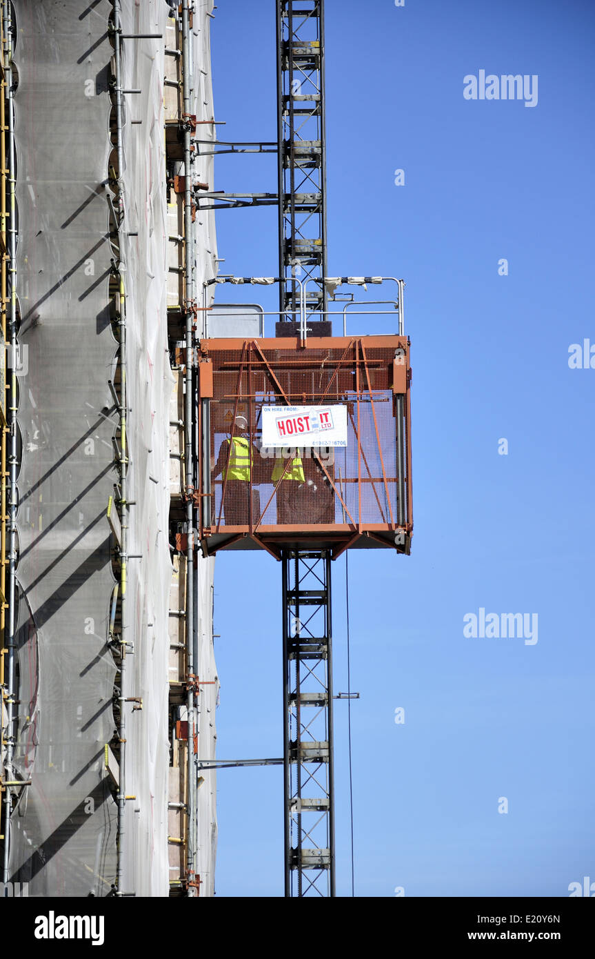 Workmen in lift hoist on outside of block of flats being renovated ...