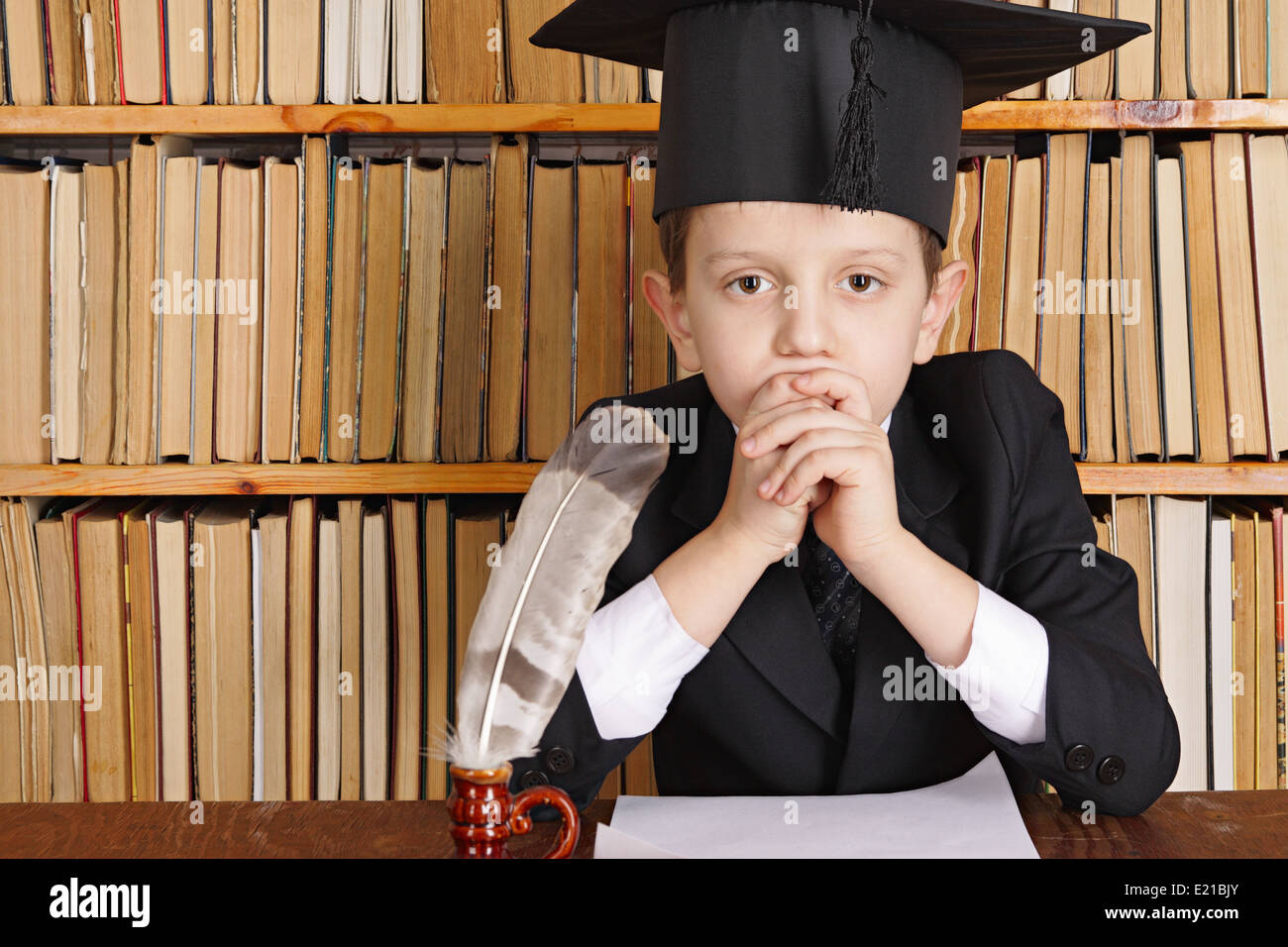 Thoughtful child as a professor with quill and paper in library Stock ...