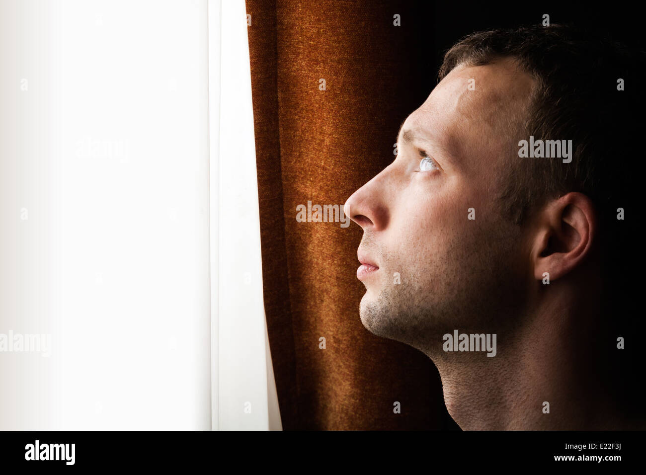 Young Caucasian man looking in bright window, closeup profile portrait ...