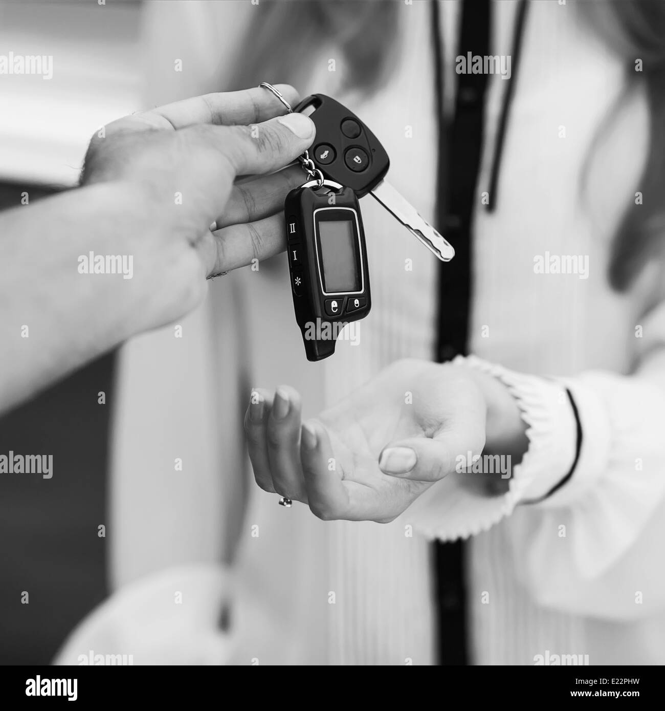 Male hand giving car key to female hand. She is holding a cell phone ...