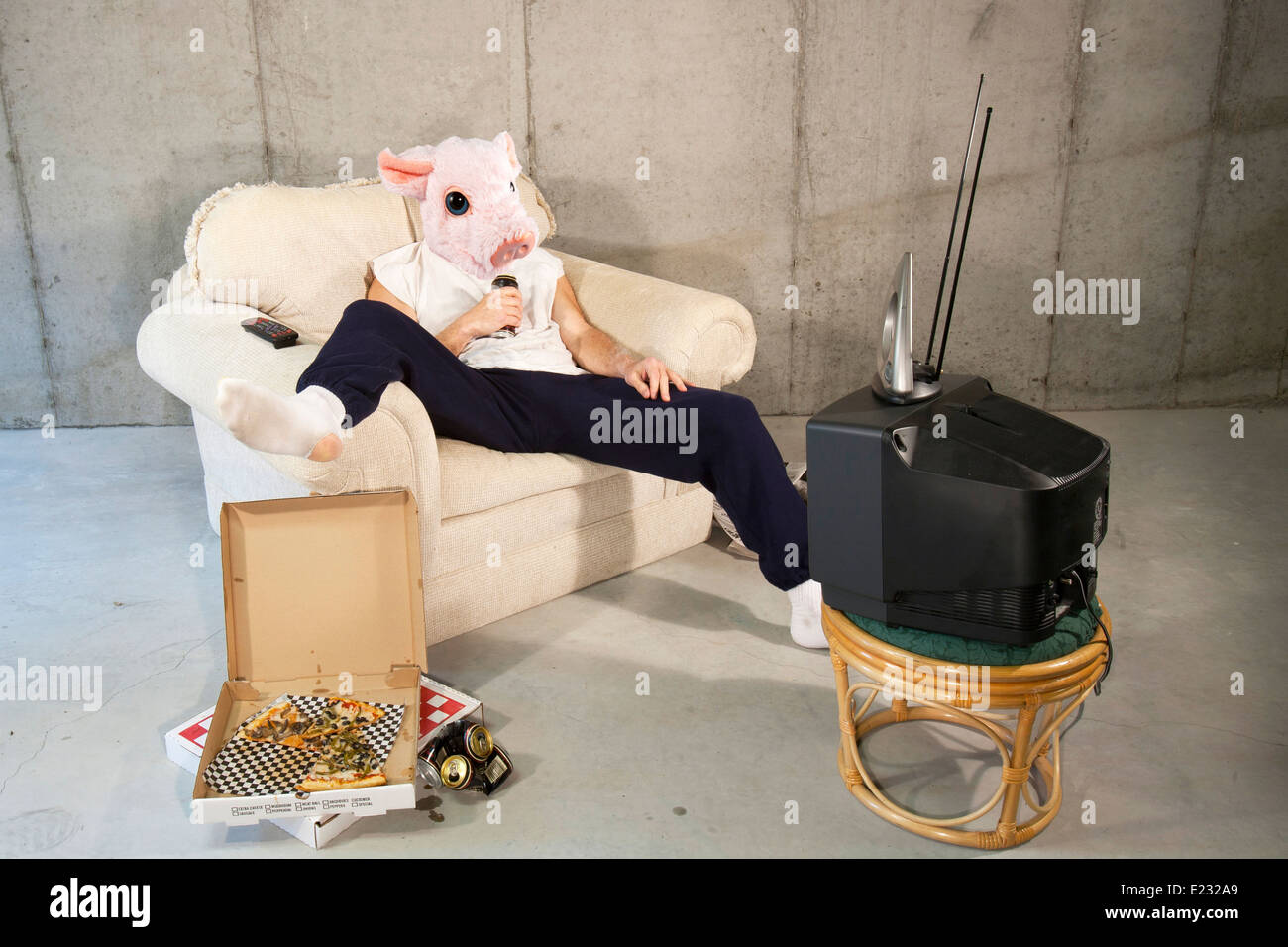 Man with pink pigs head in basement watching TV eating pizza and ...