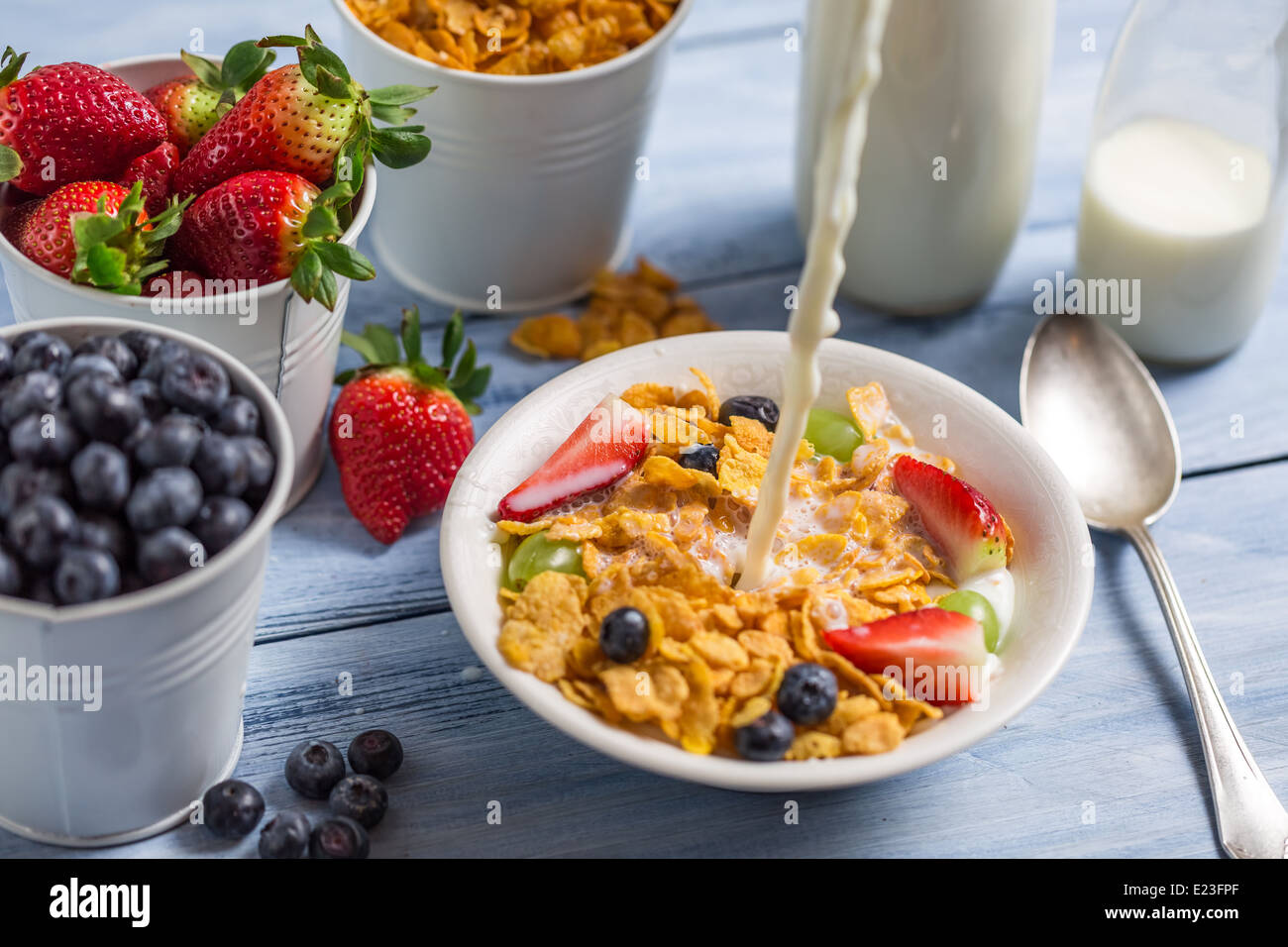Pouring milk into cornflakes with fruits Stock Photo - Alamy