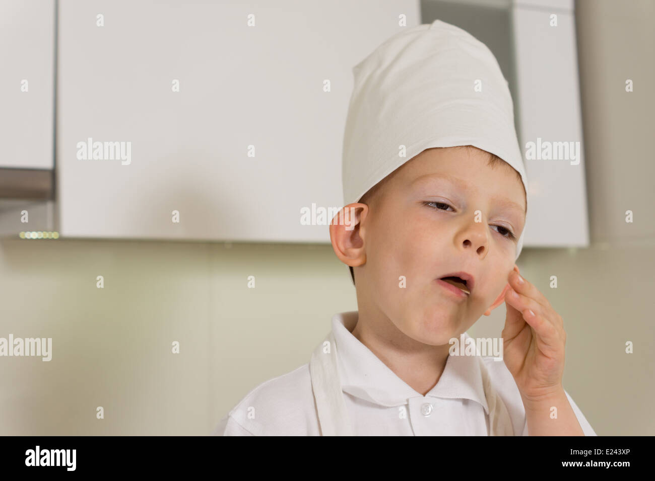 Cute little boy in a tall white chefs toque or hat cooking in the ...