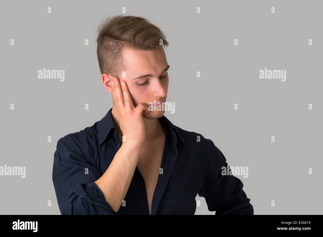 Sad, depressed blond young man looking down. Light grey background ...