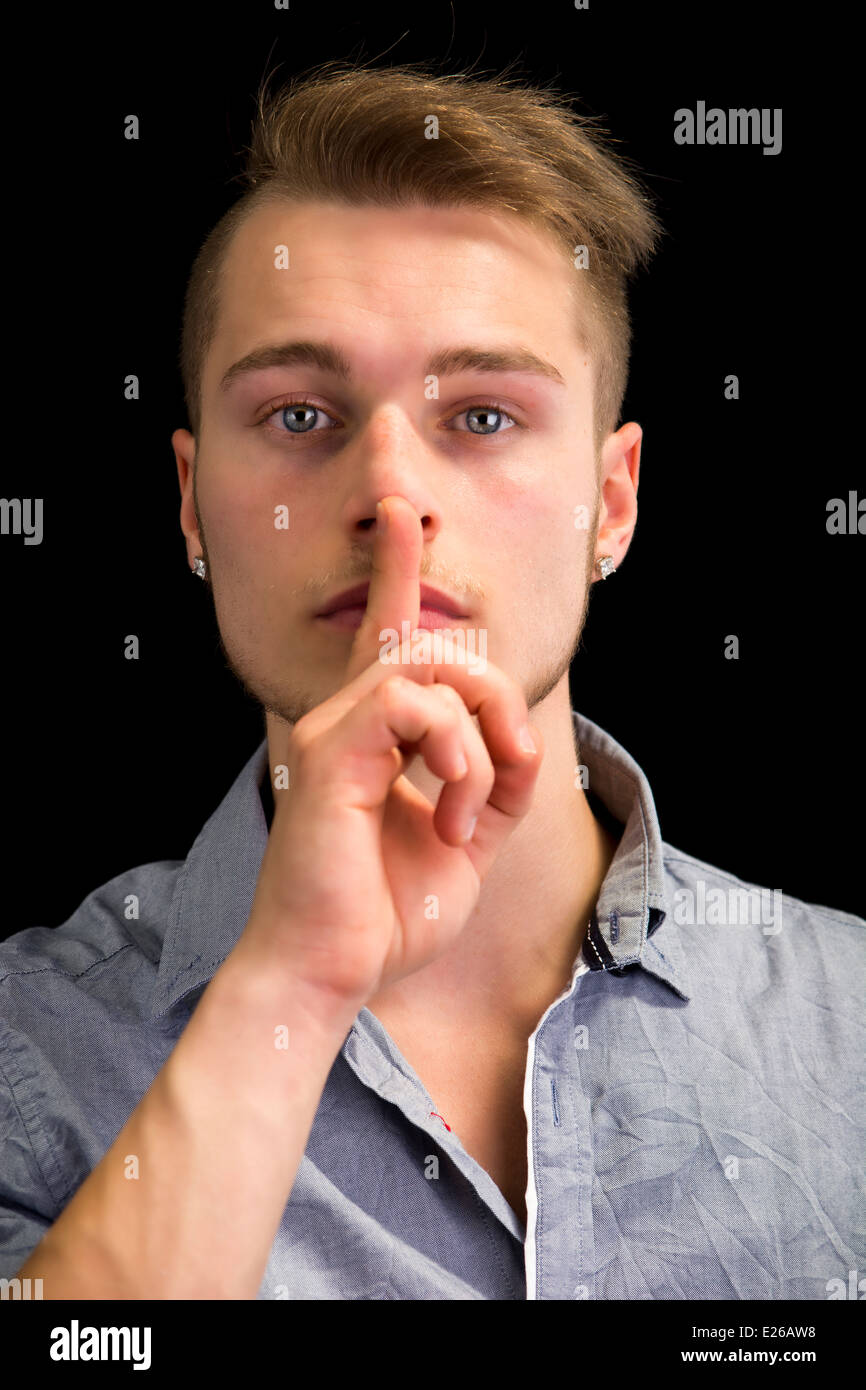 Attractive young man gesturing Hush or Silence with finger on mouth and ...