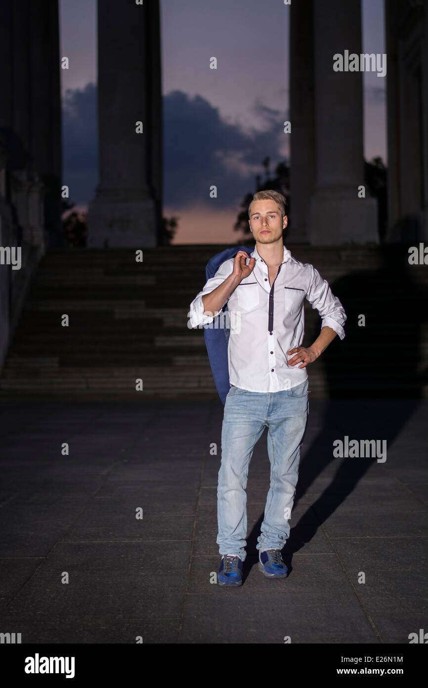 Handsome blond young man with marble columns behind him, at dusk or ...