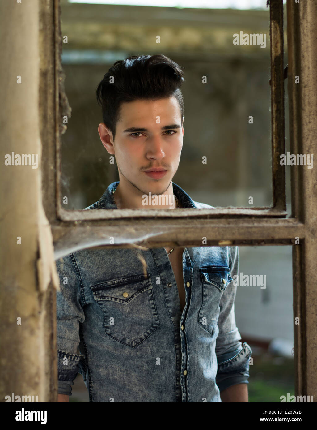 Handsome black haired young man in denim shirt in abandoned house ...