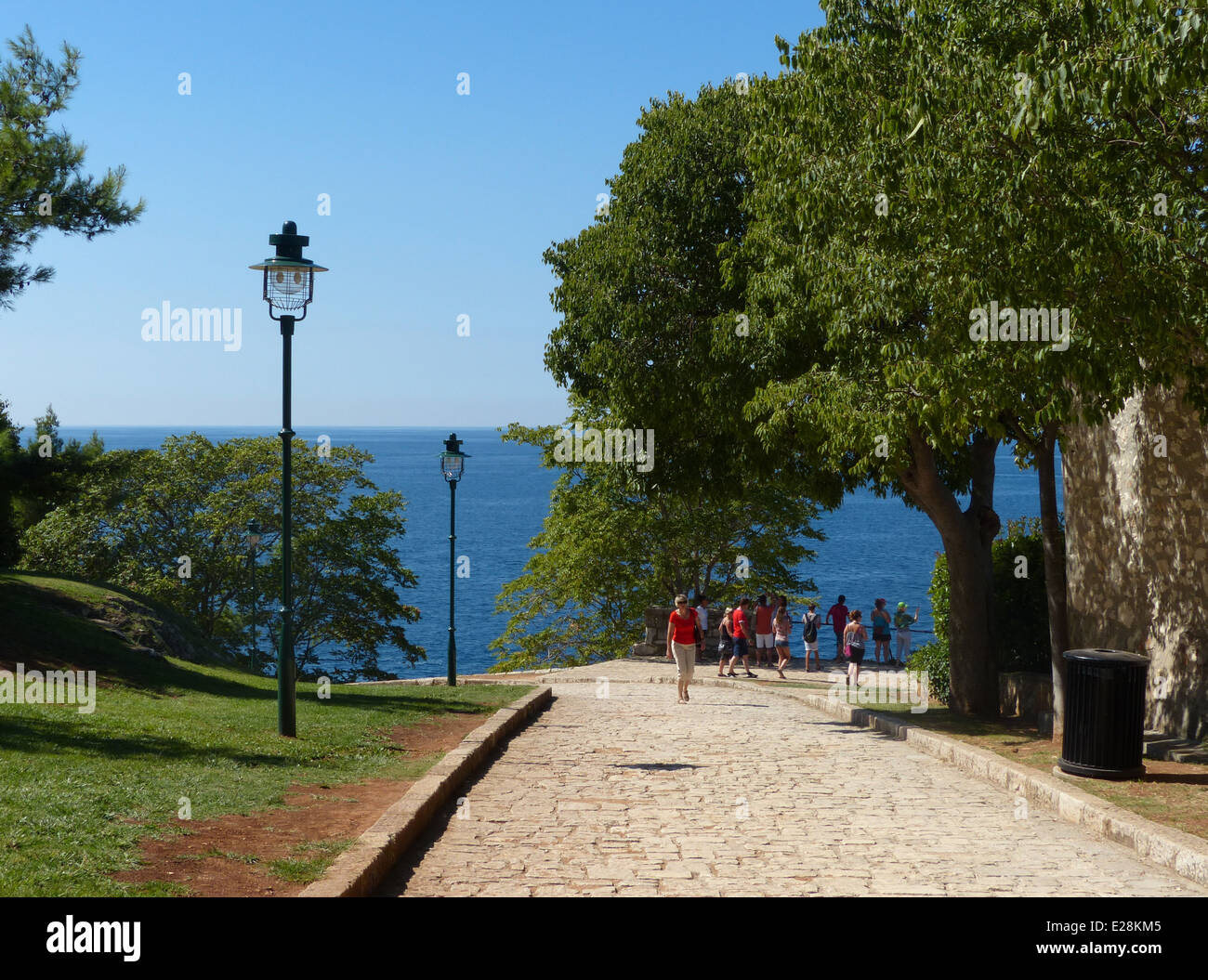 People walking up a cobbled hillside street on a sunny day with blue ...