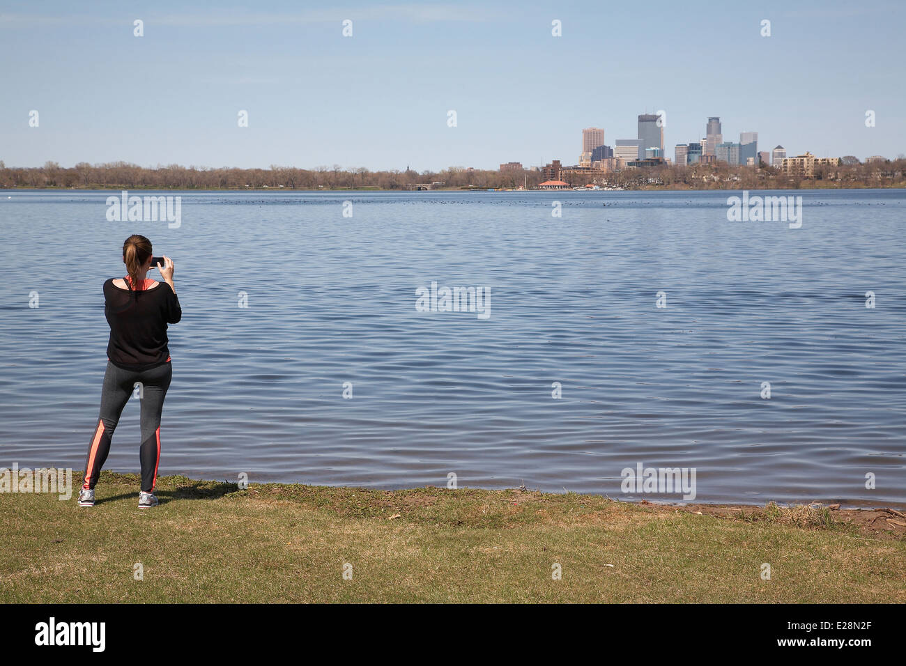 A young girl taking a picture of the city of Minneapolis across lake ...