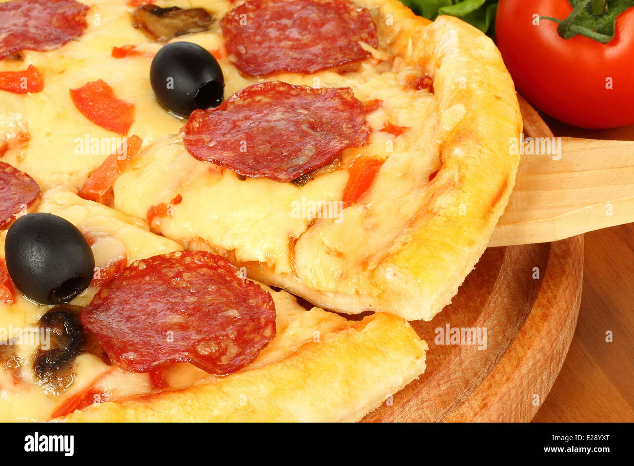 A slice of pizza is lifted from the wooden round board with a spatula ...