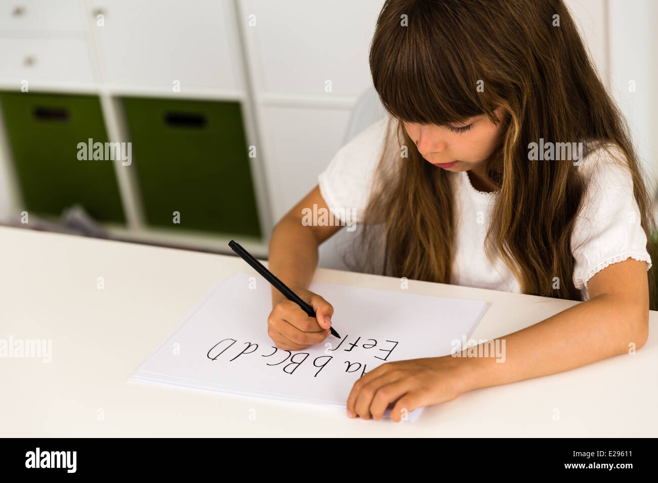 Young caucasian girl with long hair writing letters on a white piece of ...