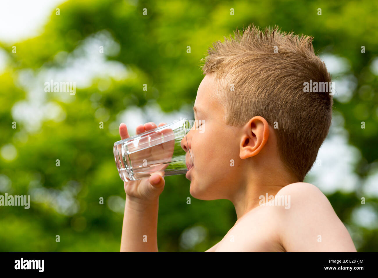 Young caucasian boy drinking from glass with fresh water outdoors ...