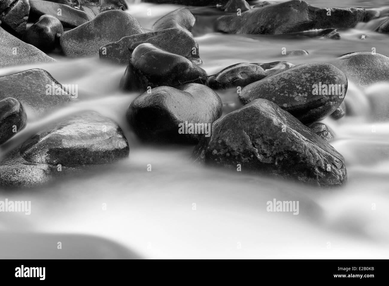 Black and white long exposure of water running over rocks in a river ...