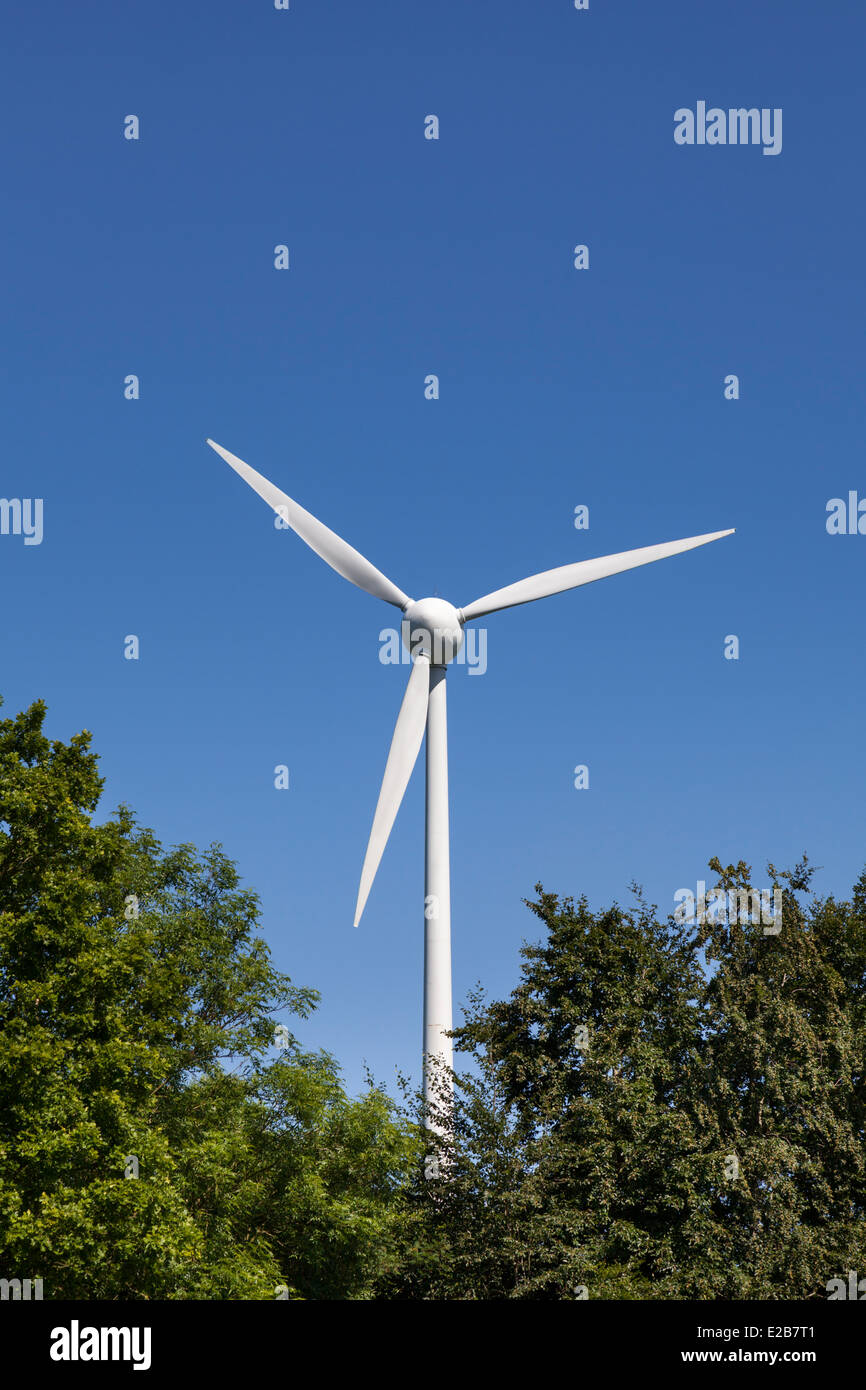 Wind turbine rotor against bright blue sky with trees in foreground ...