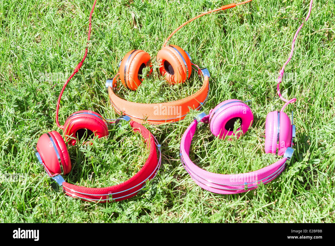 Three varicolored vibrant colorful headphones on summer sunlit green ...