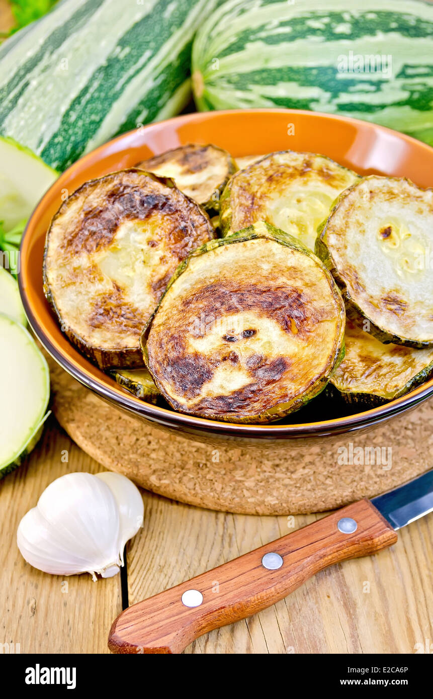 Fried zucchini in a ceramic pot, garlic, fresh zucchini, knife on ...