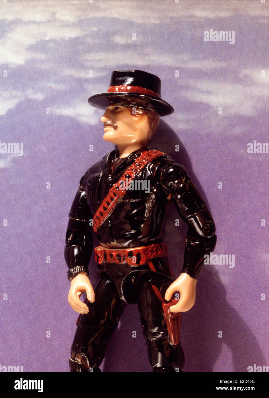 A plastic toy cowboy figure against a printed blue sky with clouds. The ...