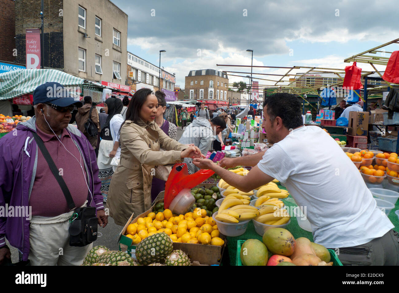 A woman customer paying a market trader on a Ridley Road Market fruit ...