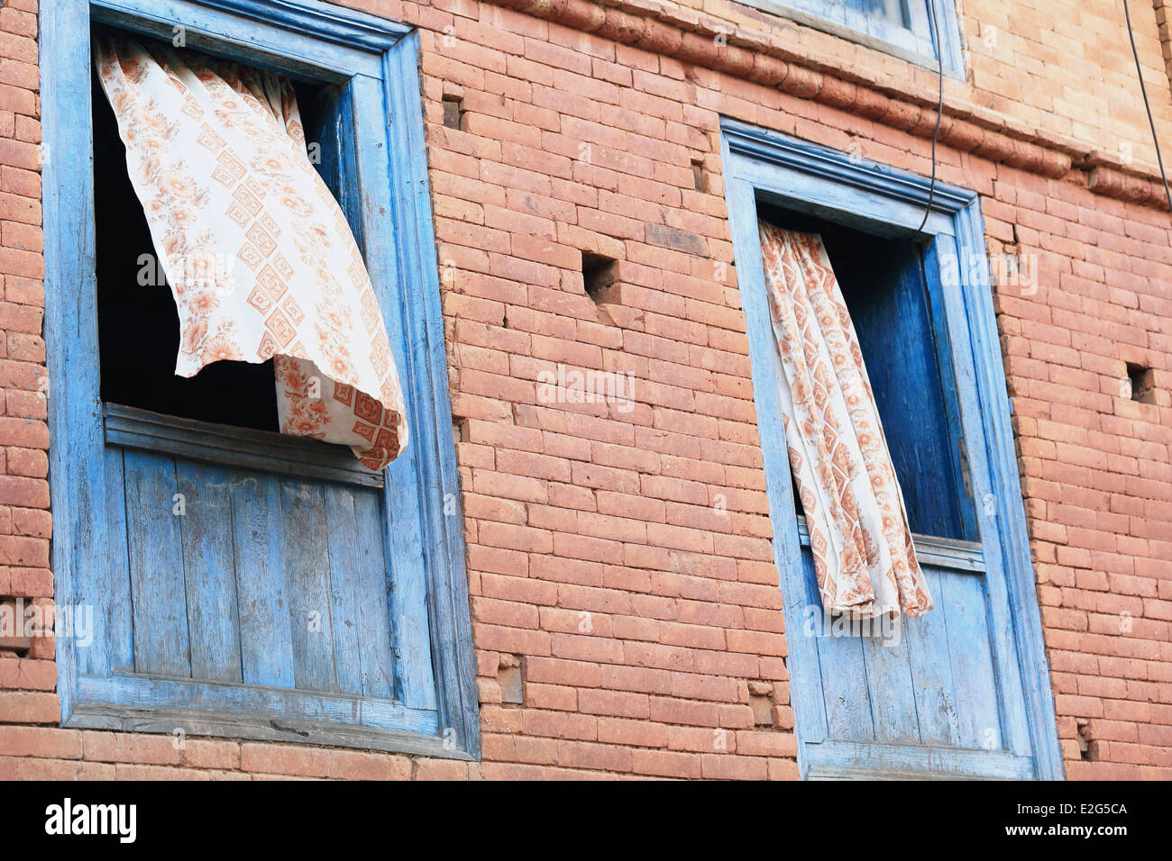 Blue painted wooden windows with waving curtains on red brick facade ...