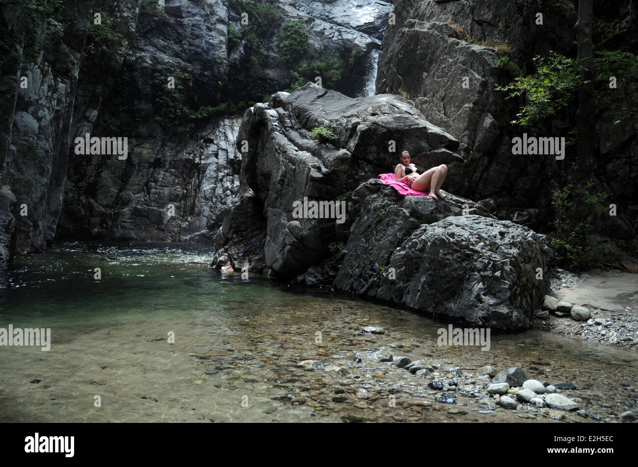 A woman lying on a rock near a waterfall on the Fonias River, on the ...