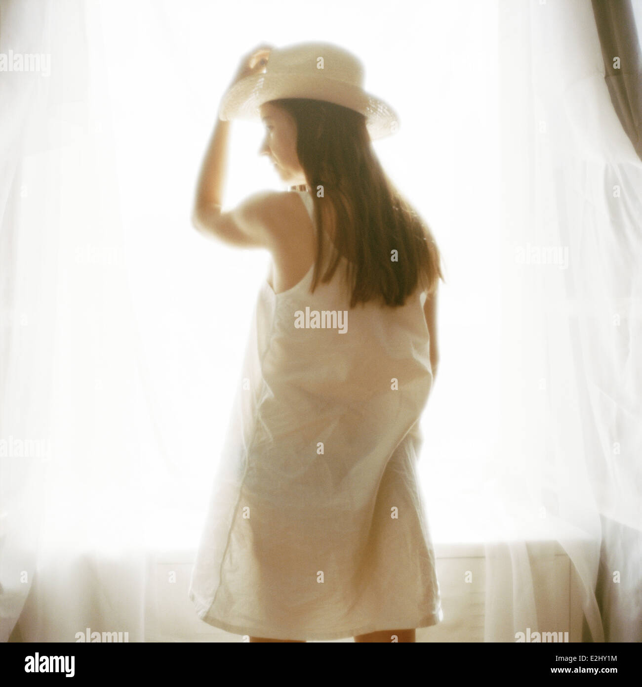 Woman putting on hat, looking out window Stock Photo - Alamy