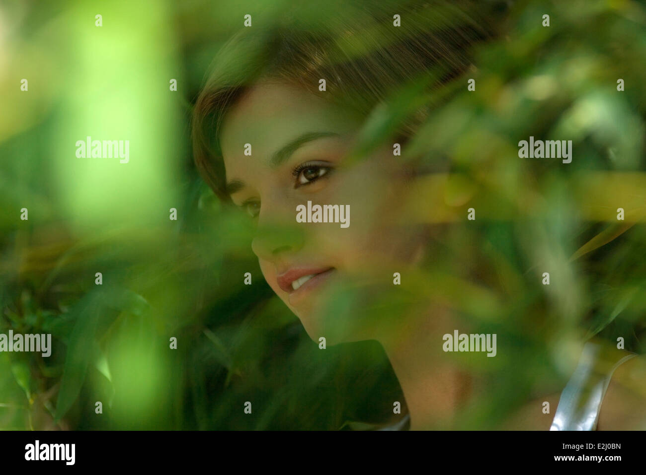 Young woman behind foliage, looking away Stock Photo - Alamy