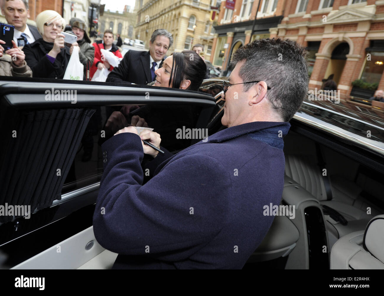 Simon Cowell appears to sign his autograph on a bank note for a waiting ...