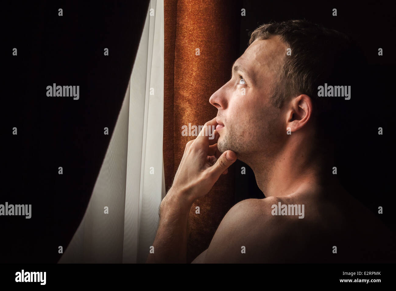 Young Caucasian man looking in the window, closeup profile portrait ...