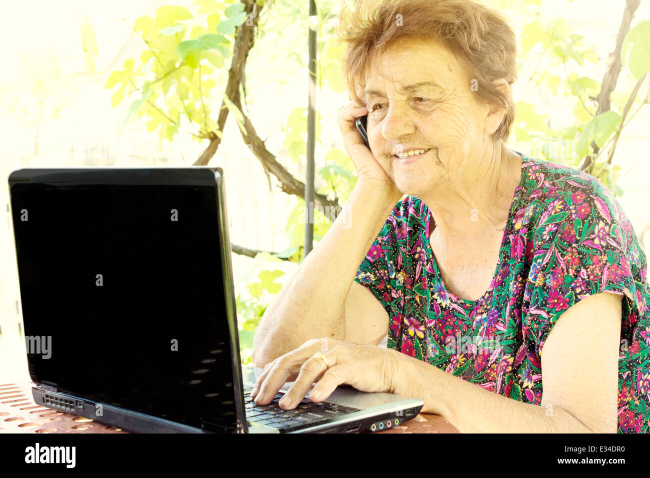 Old female using laptop computer and mobile phone Stock Photo - Alamy
