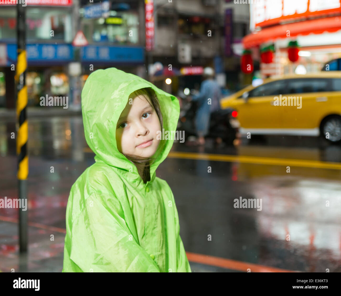Young girl in rain wearing a green raincoat next to a city street Stock ...