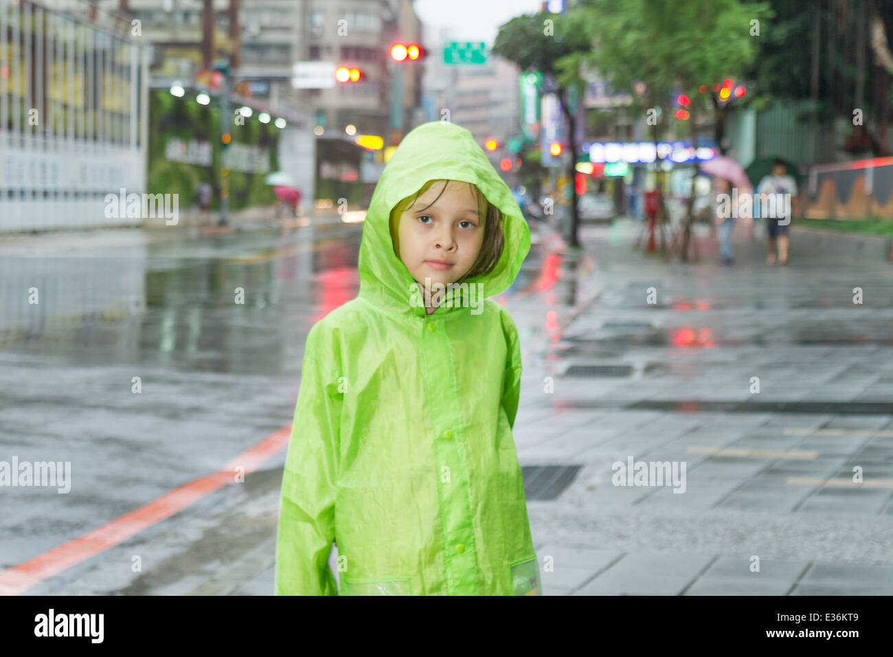 Young girl in rain wearing a green raincoat next to a city street Stock ...