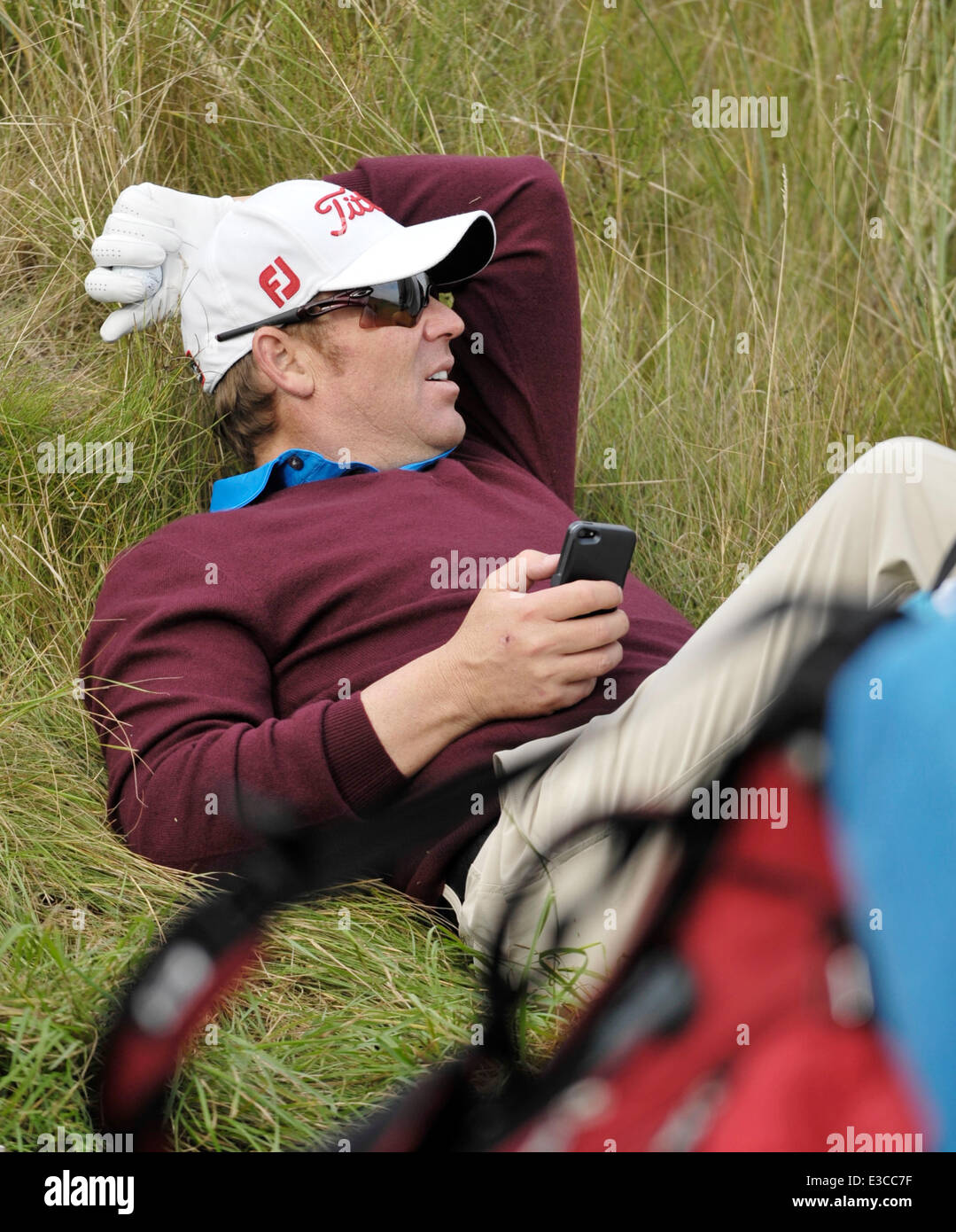 Shane Warne checks his cell phone between shots in the Alfred Dunhill ...