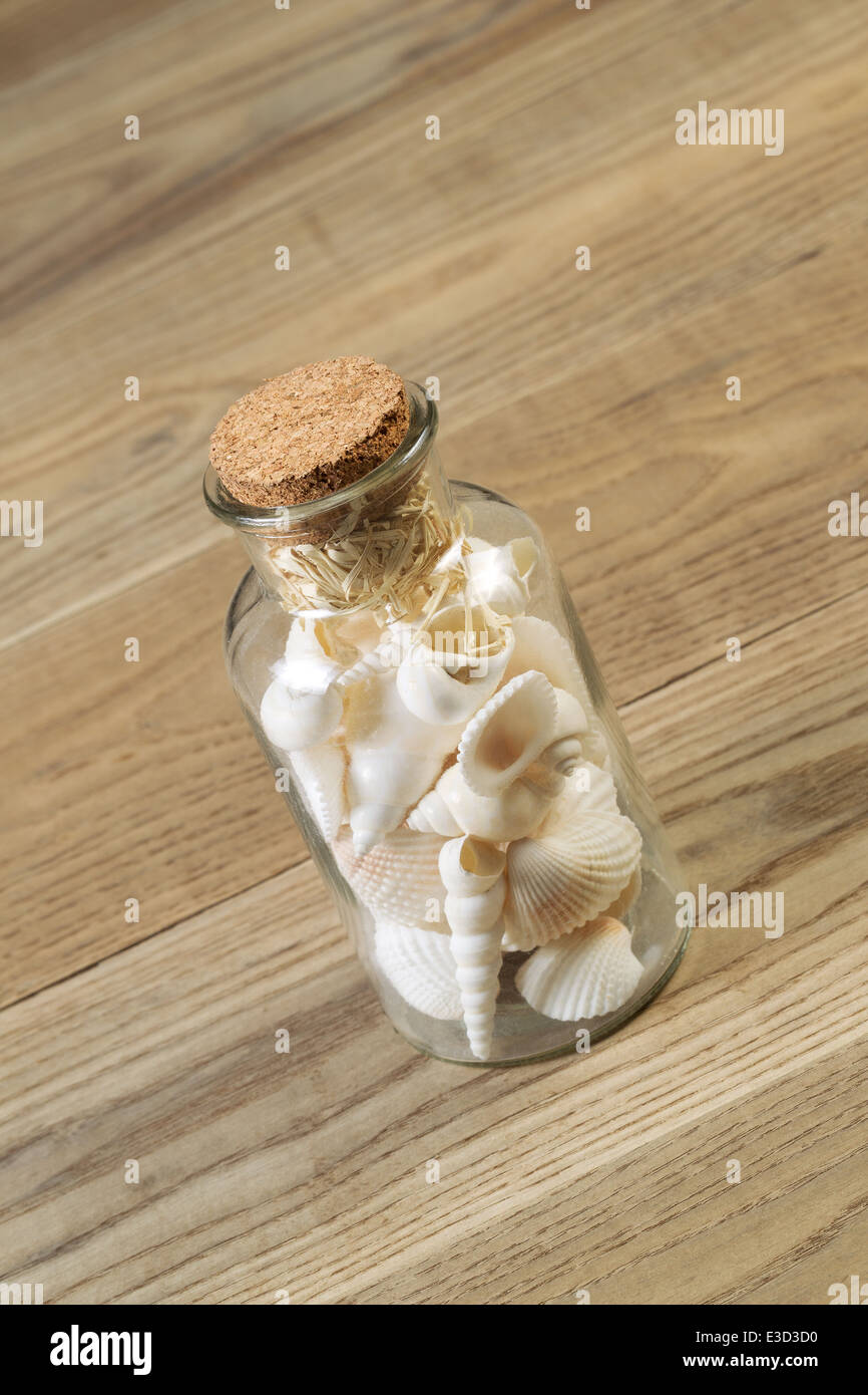 Angled vertical view of a glass bottle filled with sea shells on rustic ...