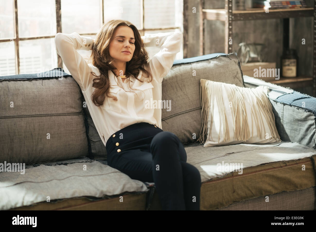 Relaxed young woman sitting in loft apartment Stock Photo - Alamy