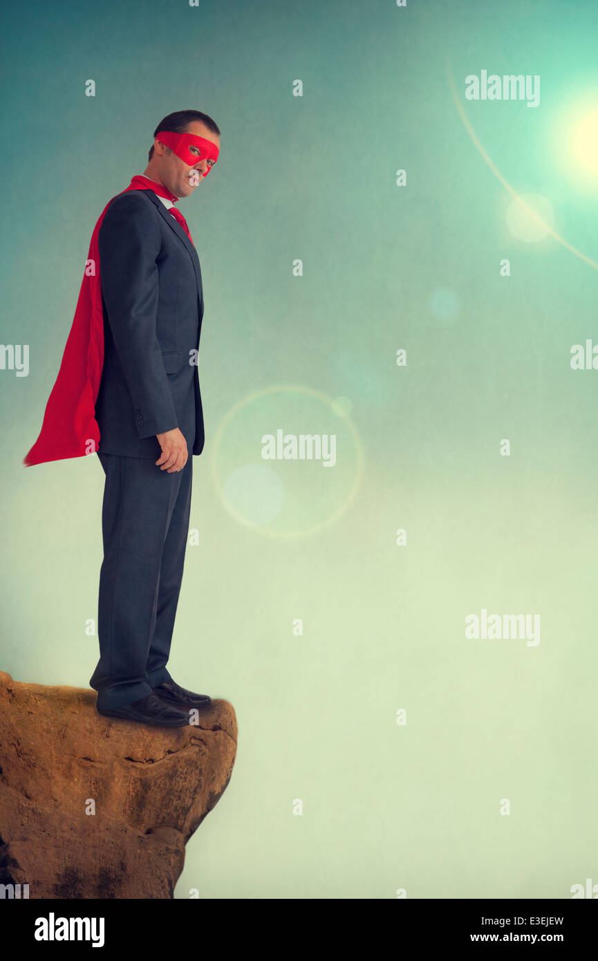 superhero businessman standing on a cliff ledge or precipice wearing ...