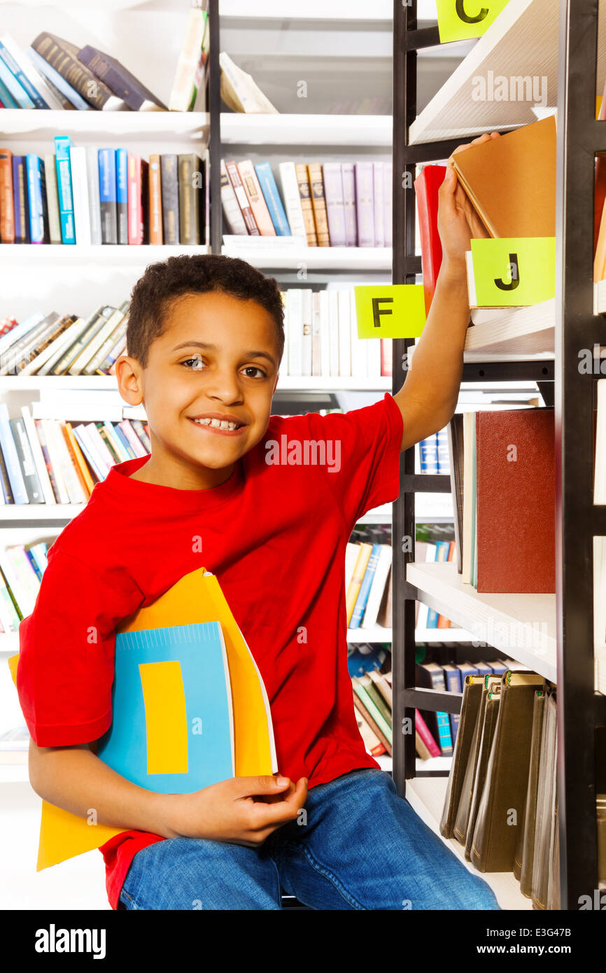 Smiling boy with hand on bookshelf holds books Stock Photo - Alamy