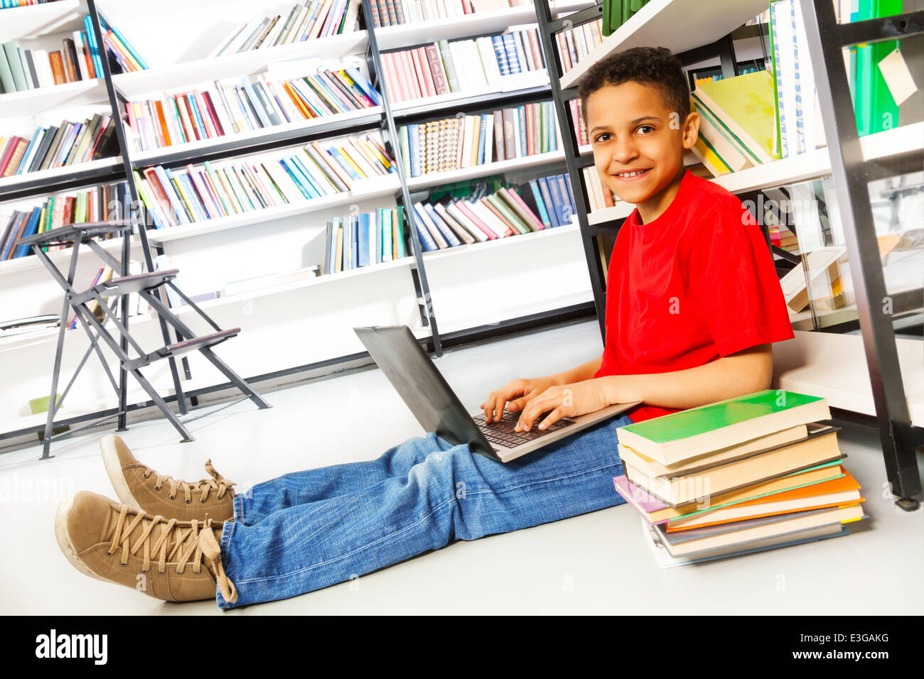 Smiling boy with books and laptop in library Stock Photo - Alamy
