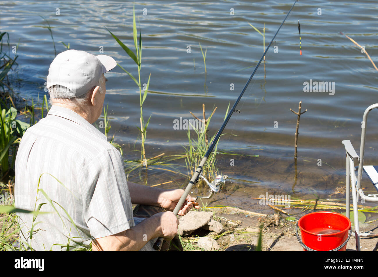 Elderly man enjoying a days fishing on a lagoon or lake sitting with ...