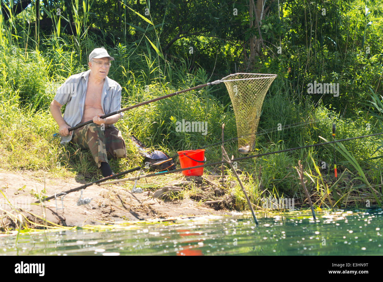 Elderly disabled fisherman with one leg using a net to land a fish as ...