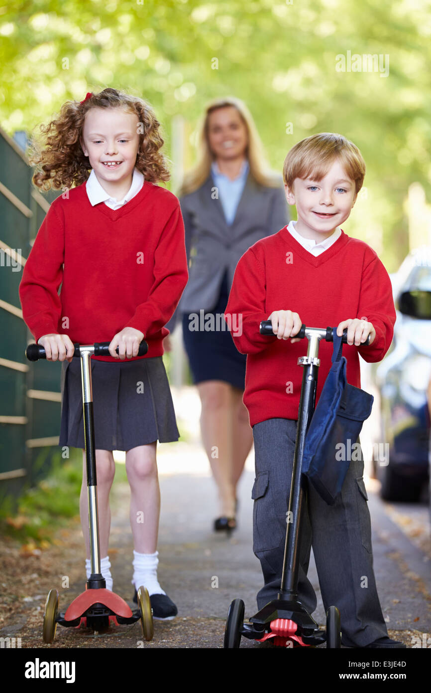 Children Riding Scooters On Their Way To School With Mother Stock Photo ...