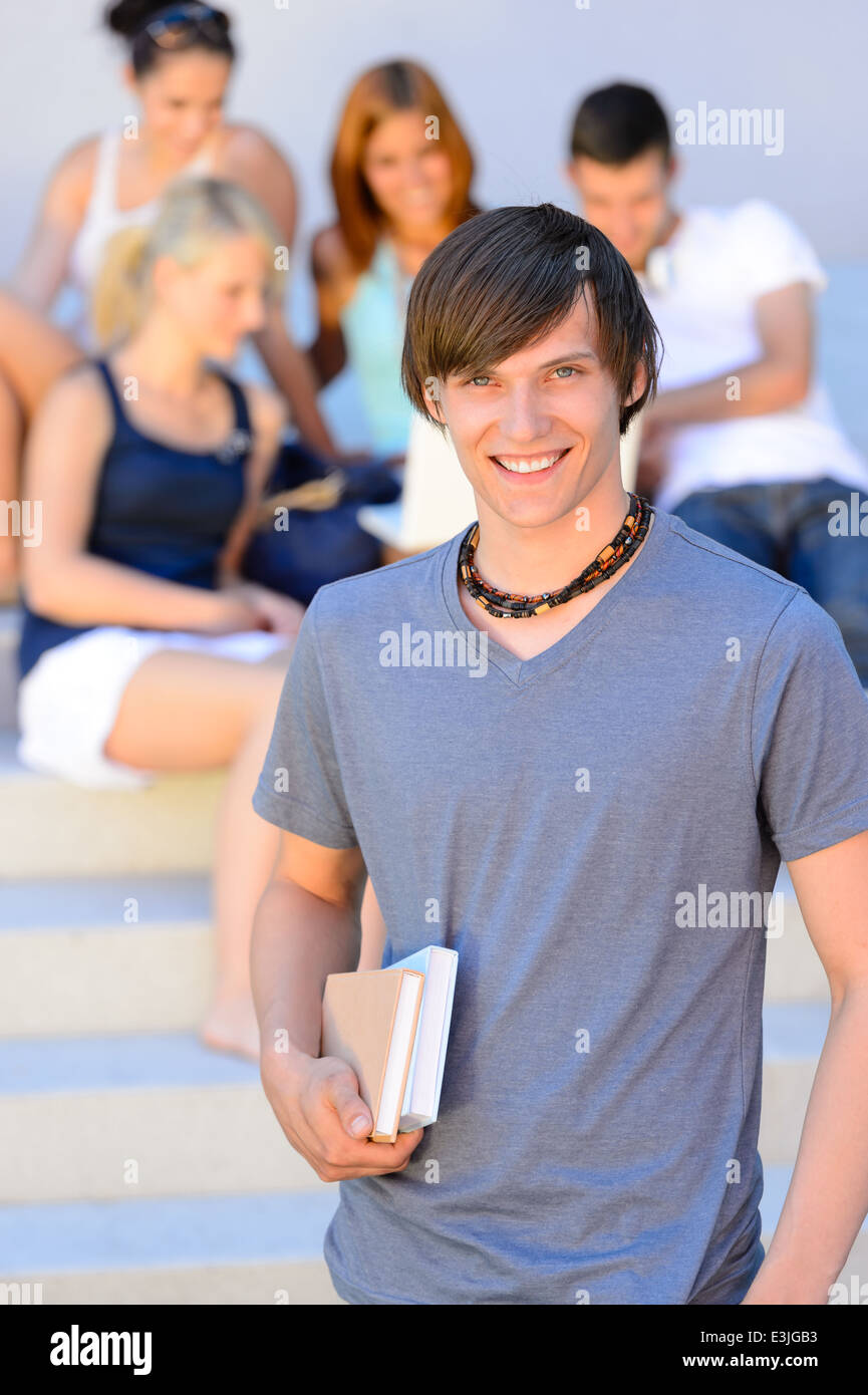 Smiling college student boy holding books friends in background summer ...