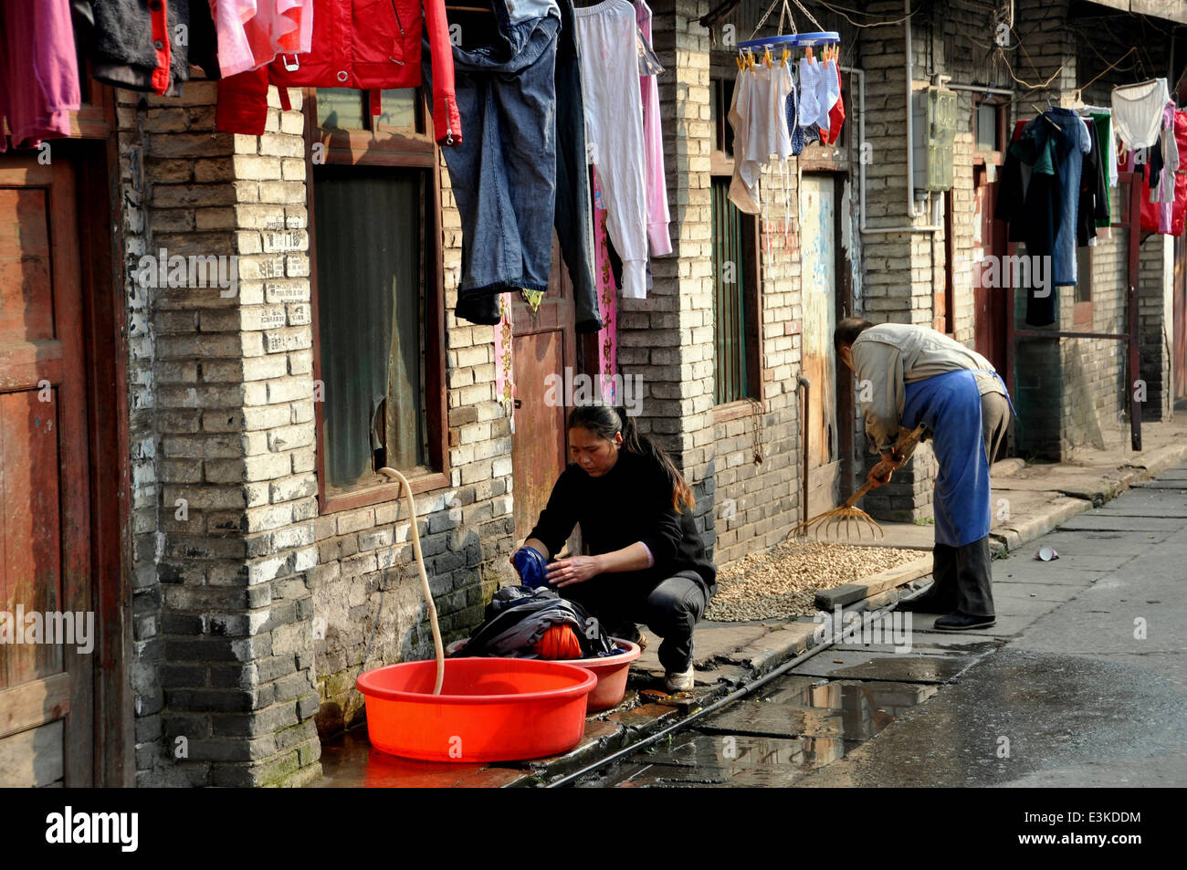 PENGZHOU, CHINA: Woman washing clothes while man rakes peanuts left ...
