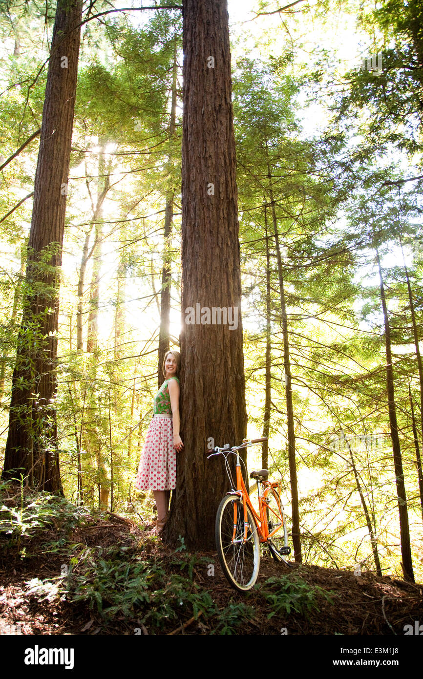 Woman leaning against tree in forest Stock Photo - Alamy