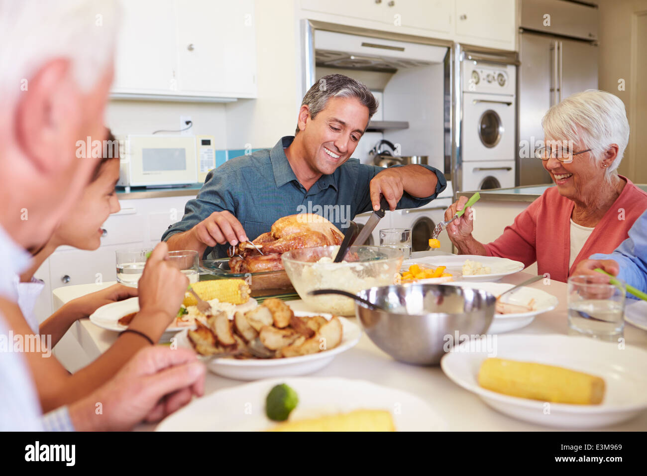 Multi-Generation Family Sitting Around Table Eating Meal Stock Photo ...