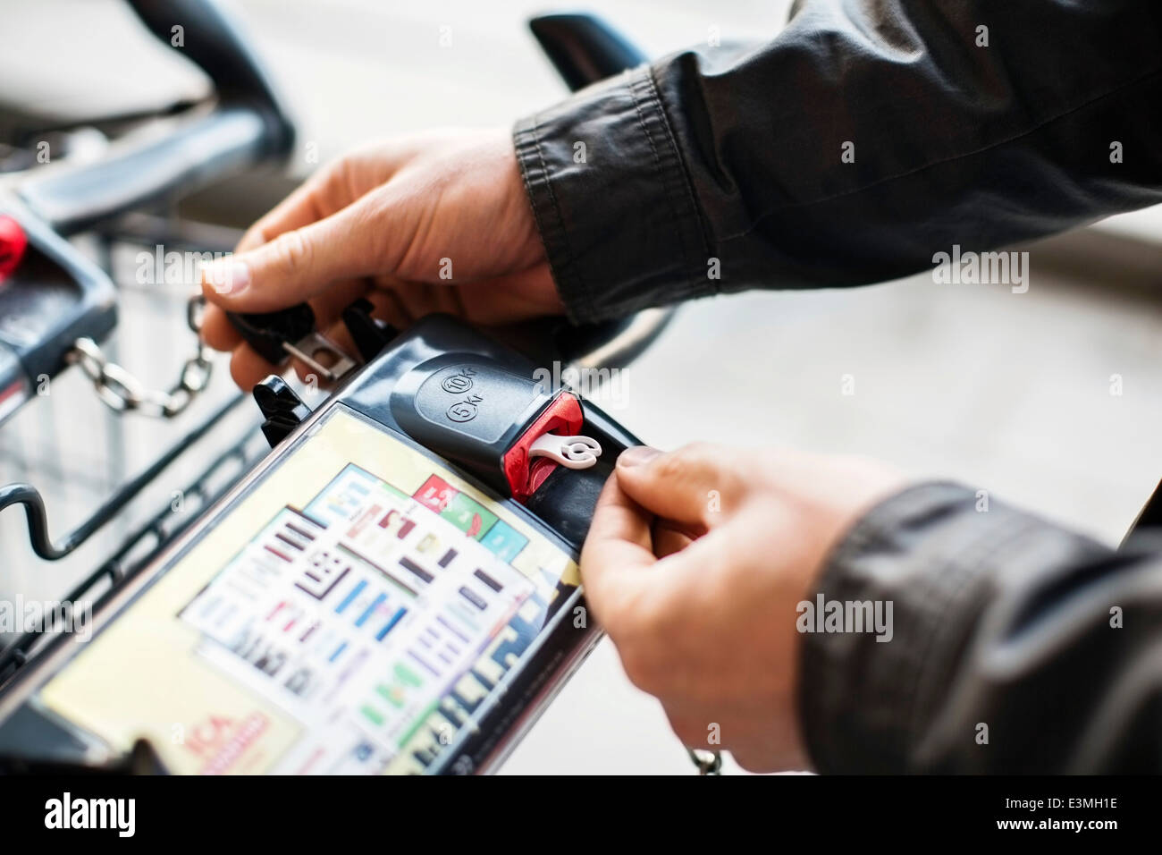 Cropped image of man removing chain from shopping cart in supermarket ...
