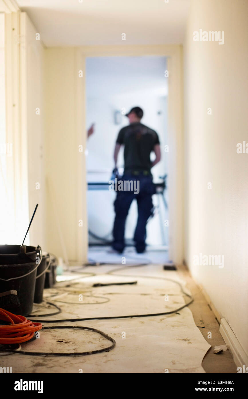 Rear view of carpenter standing at doorway in house under construction ...