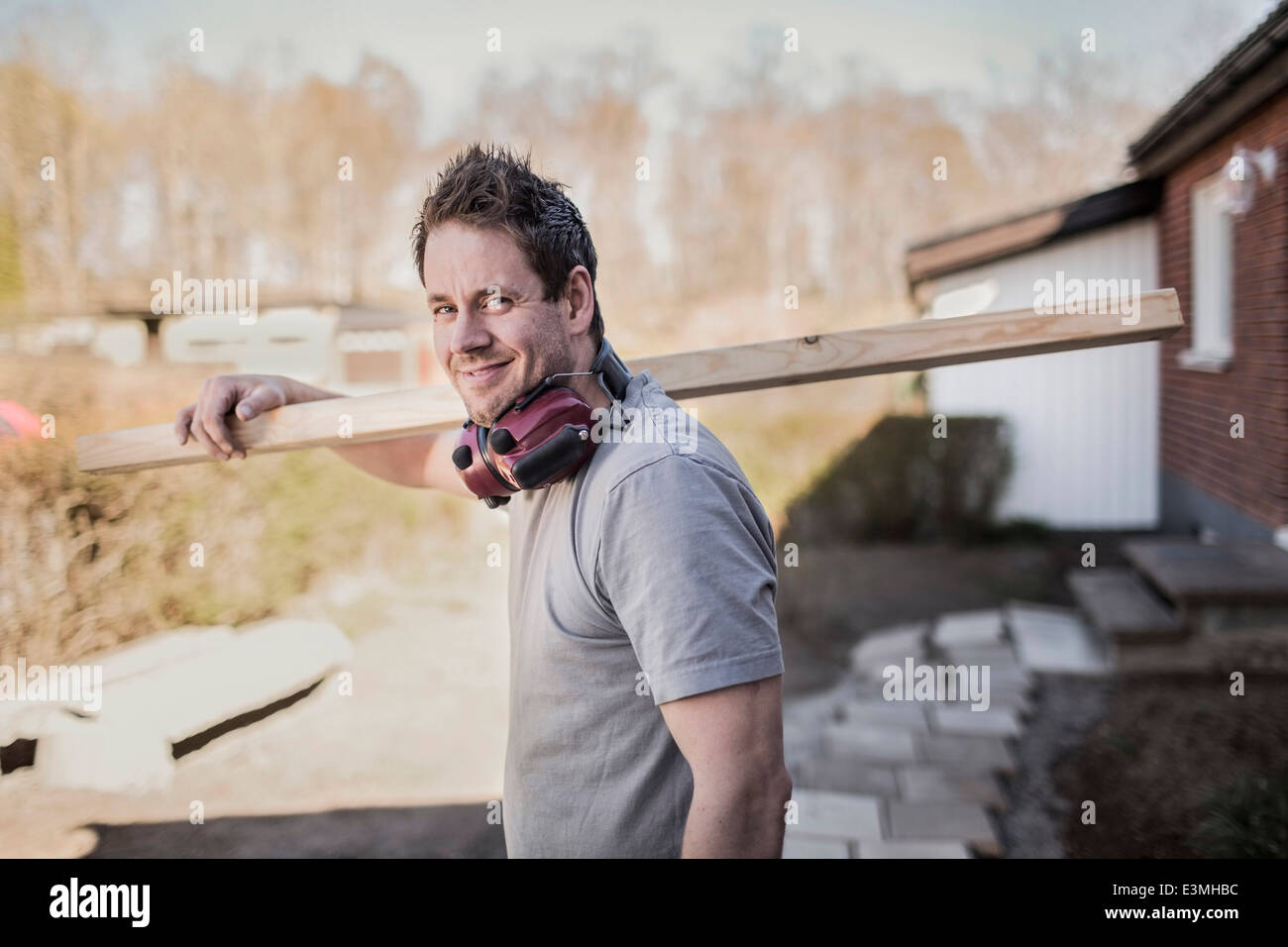 Side view portrait of smiling carpenter carrying wooden plank at ...
