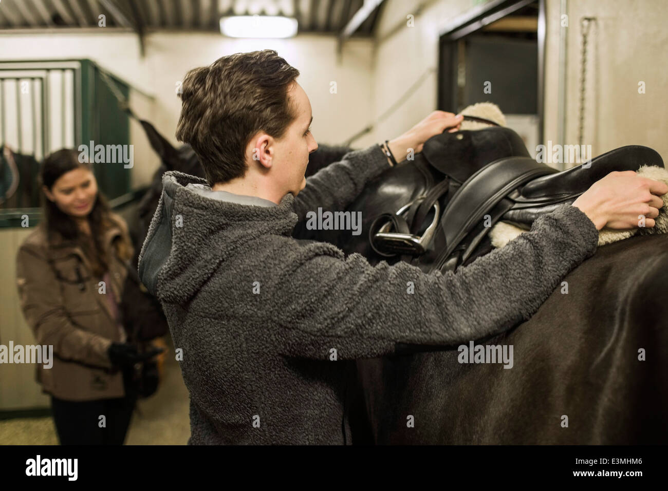 Young man preparing horse in stable with woman in background Stock ...