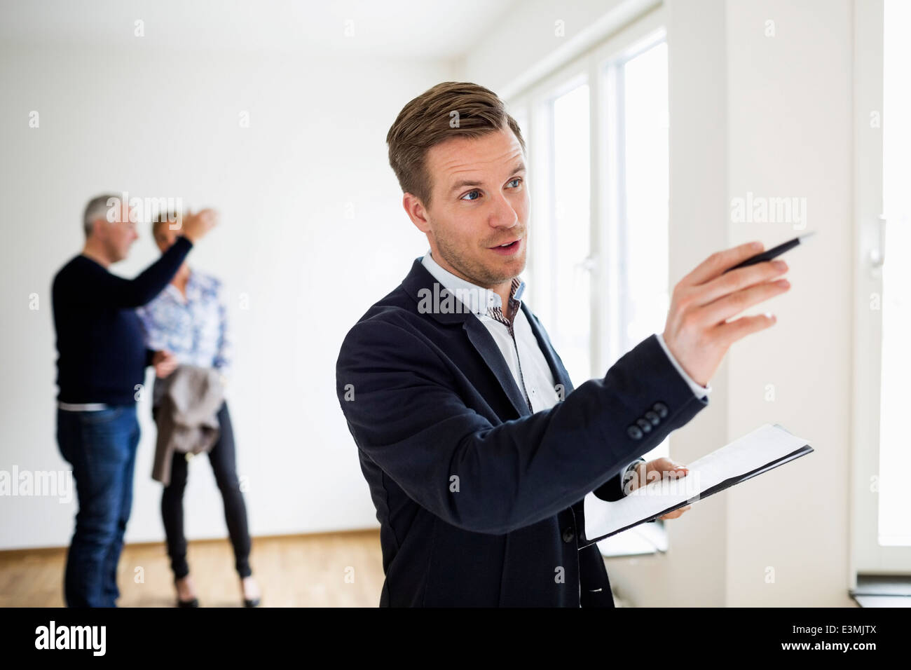 Real estate agent examining house with couple discussing in background ...