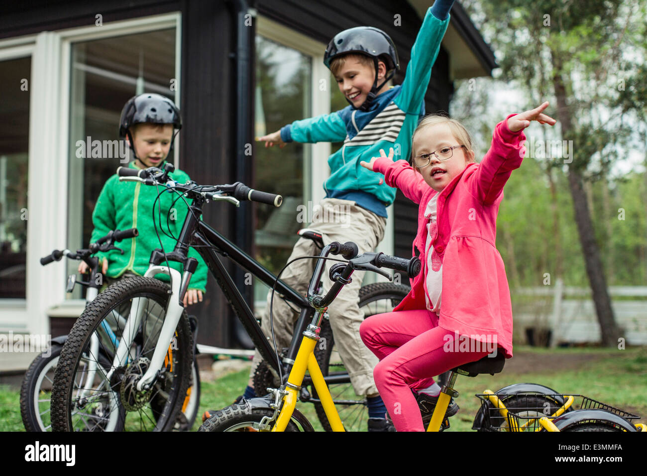 Portrait of girl with arms outstretched riding bicycle with brothers in ...